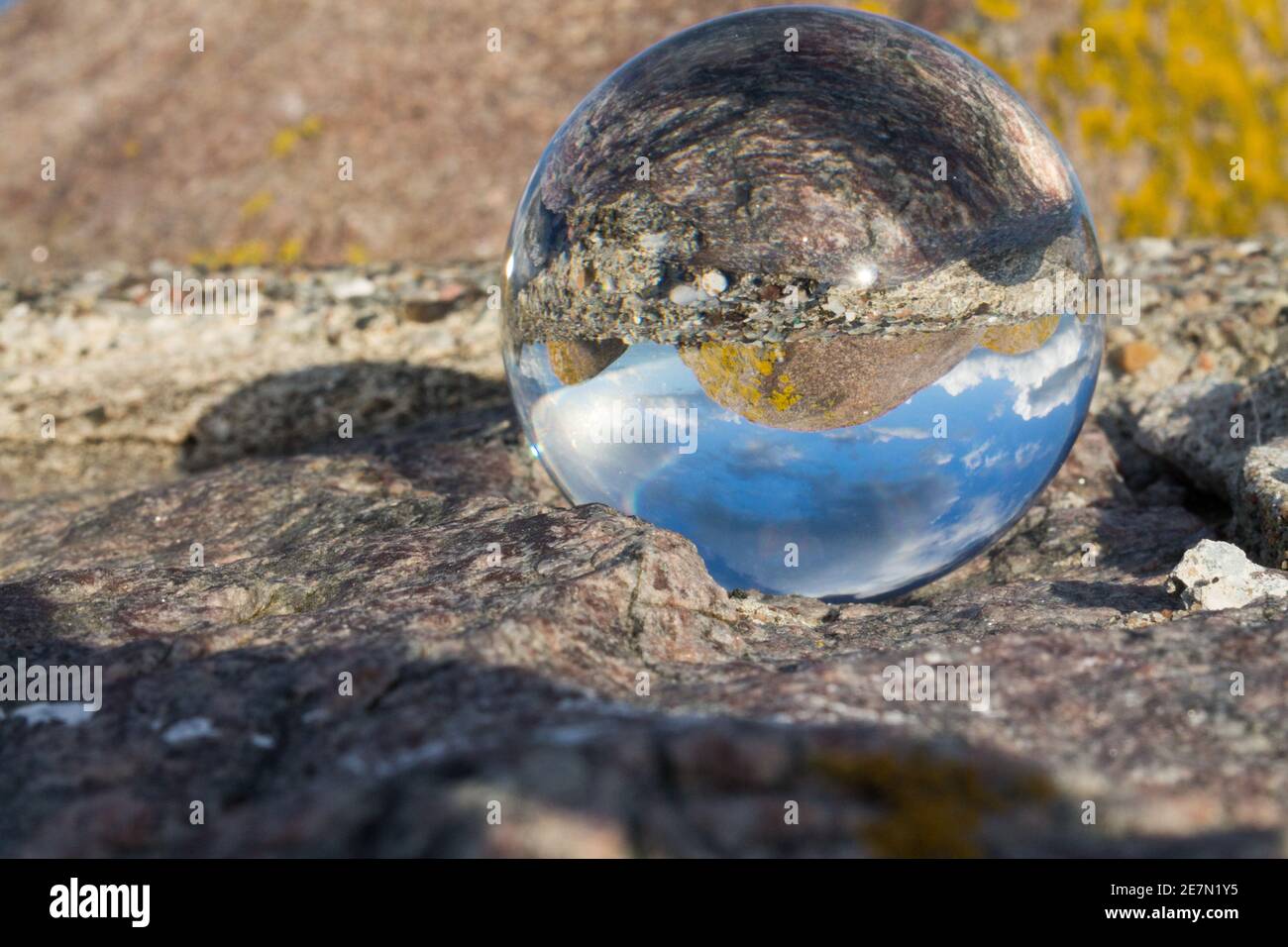 A crystal ball resting on a rocky surface reflects the bright blue sky ...
