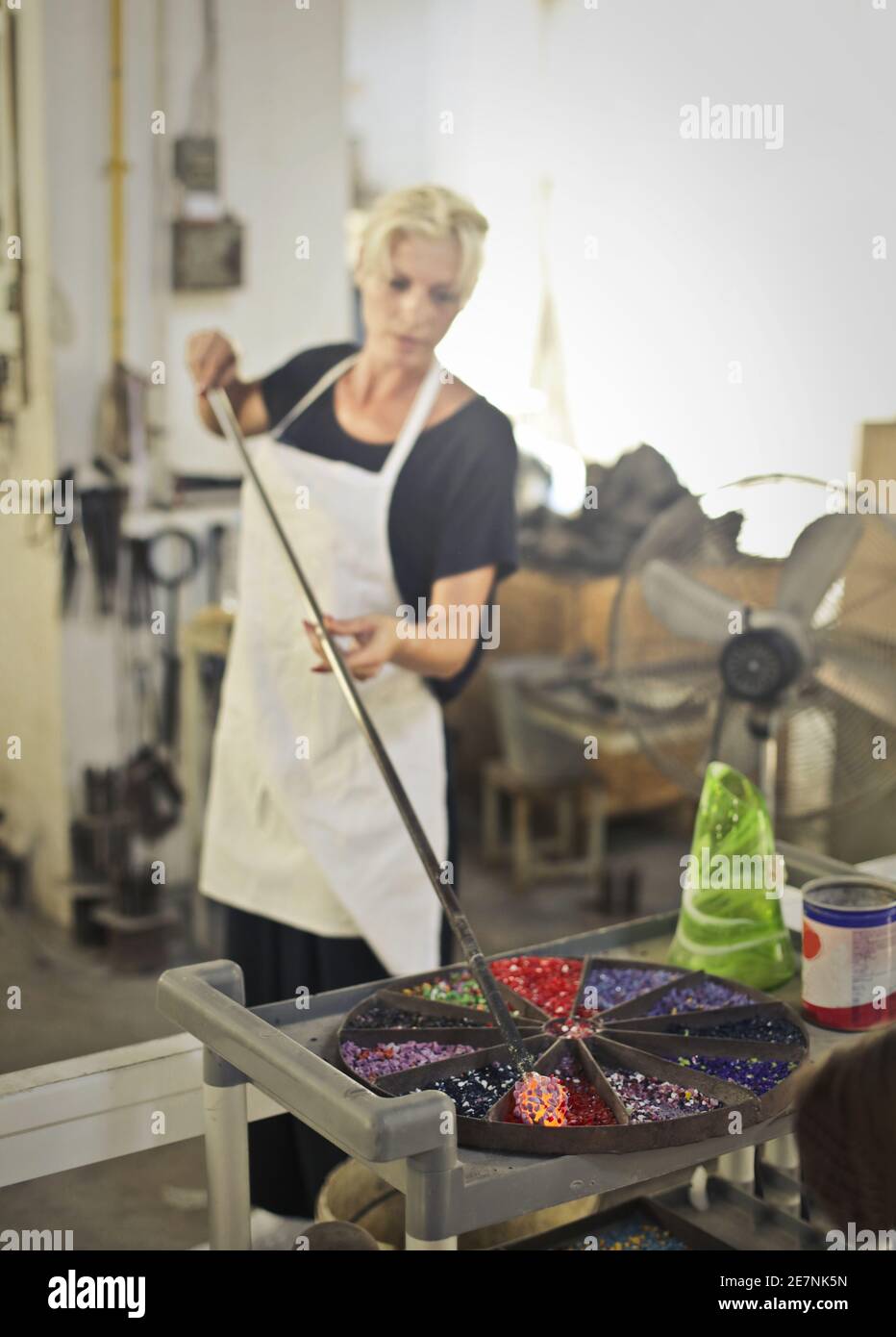 Blonde woman shaping the hot glass with tools in the glass factory ...