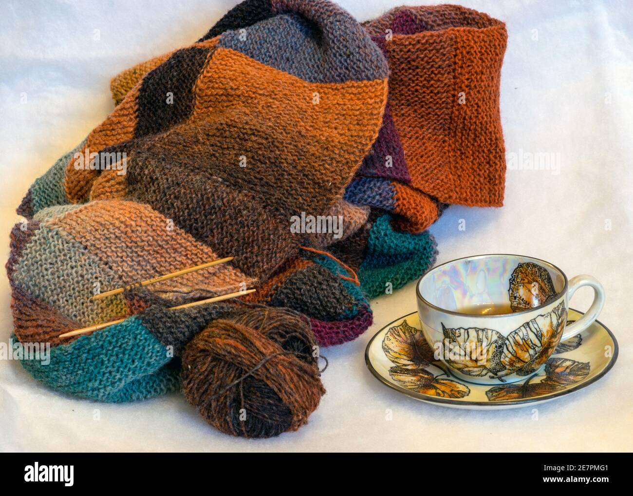 colorful knitted scarf with knitting needles, yarn ball and teacup ...