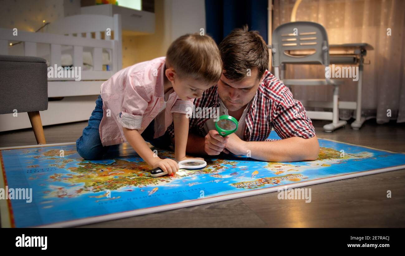 Little boy with father lying on floor and looking on big world map ...