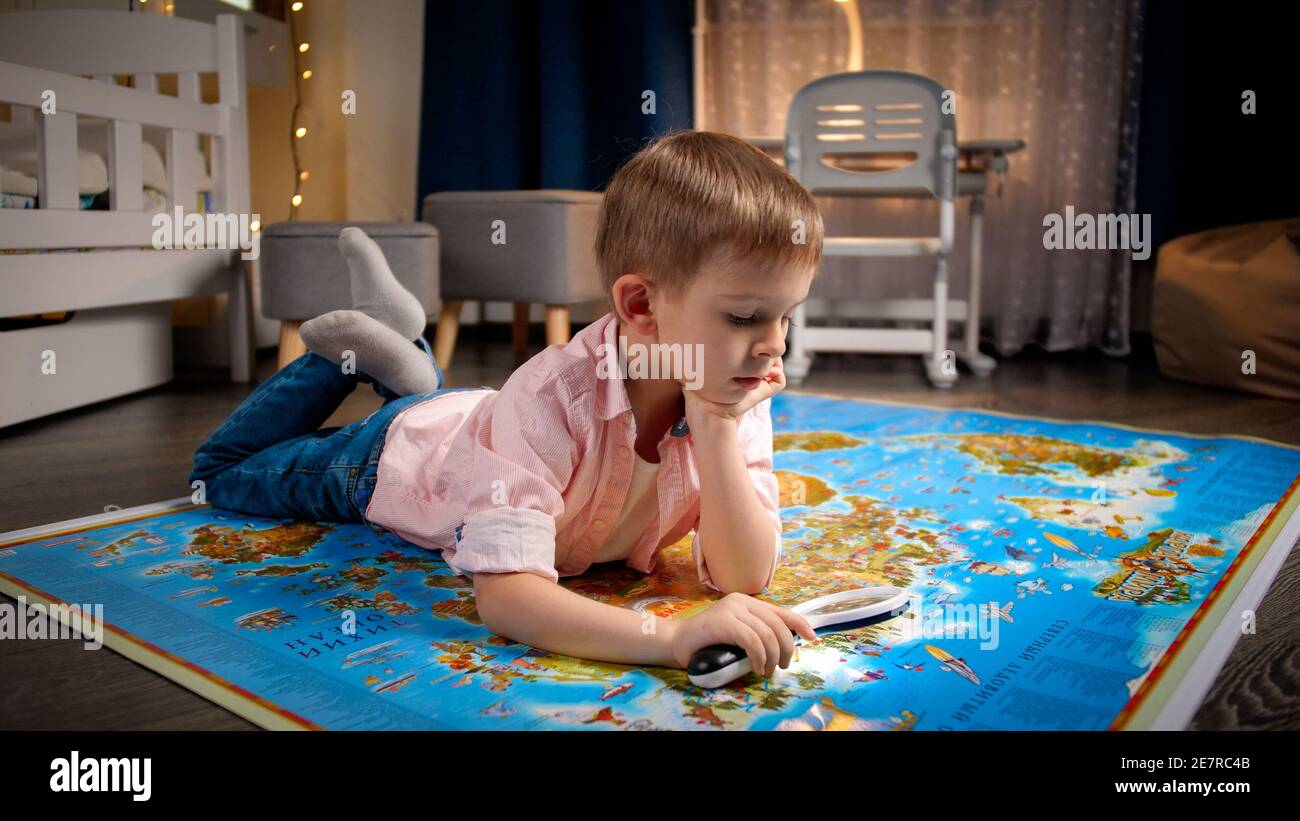 Little boy lying on floor at night and exploring big world map .Concept ...