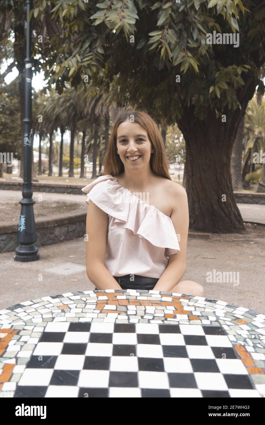 Happy Hispanic female posing in the city park by the stone table with a ...