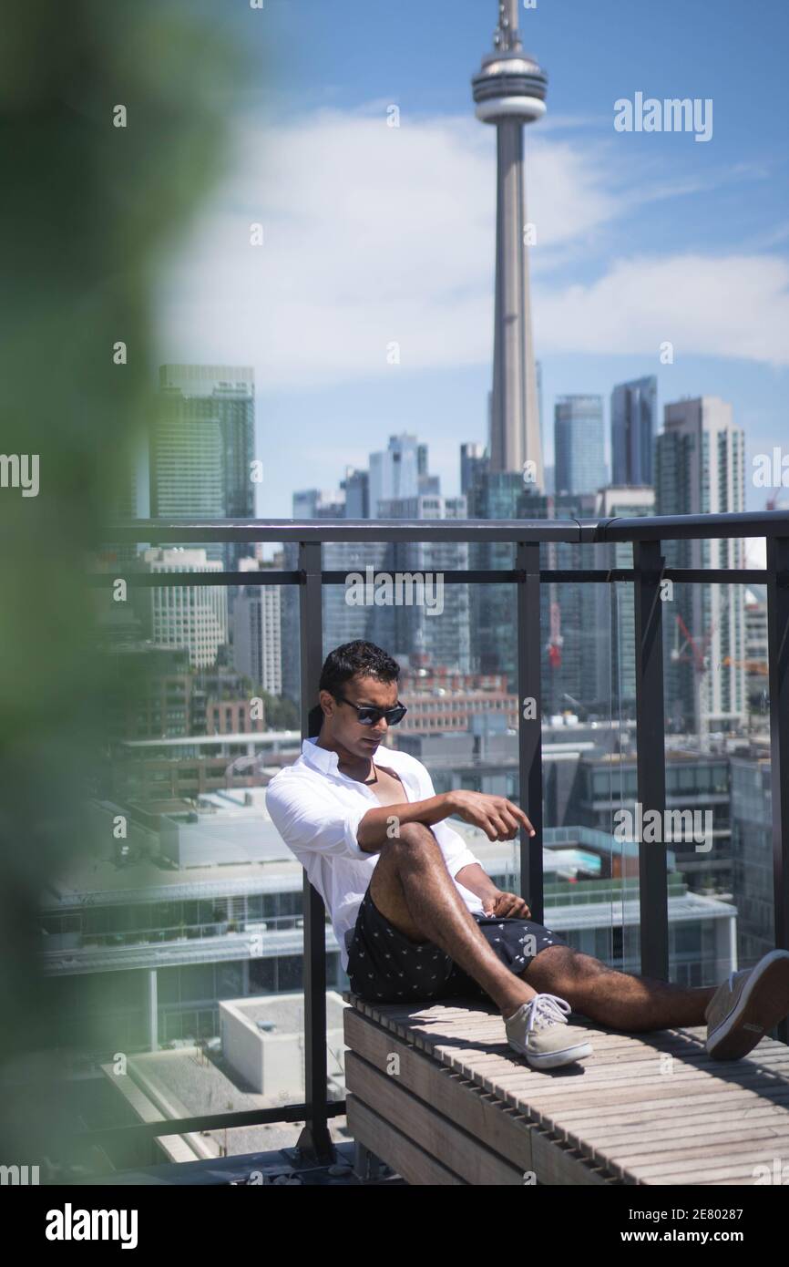 Man sitting on a bench on a rooftop patio relaxing over a Toronto view ...