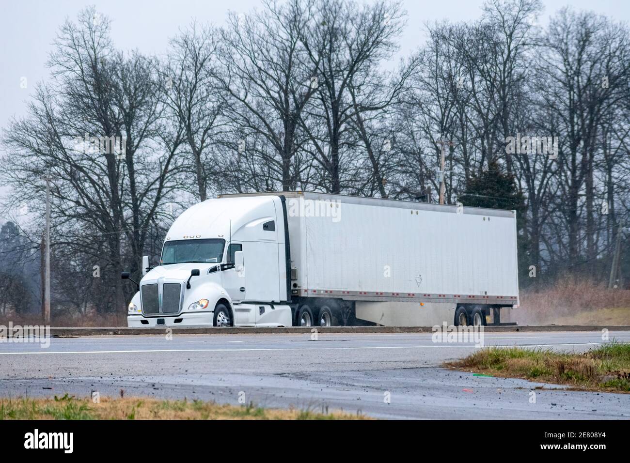 Horizontal shot of a generic white tractor trailer drives in mixed rain ...