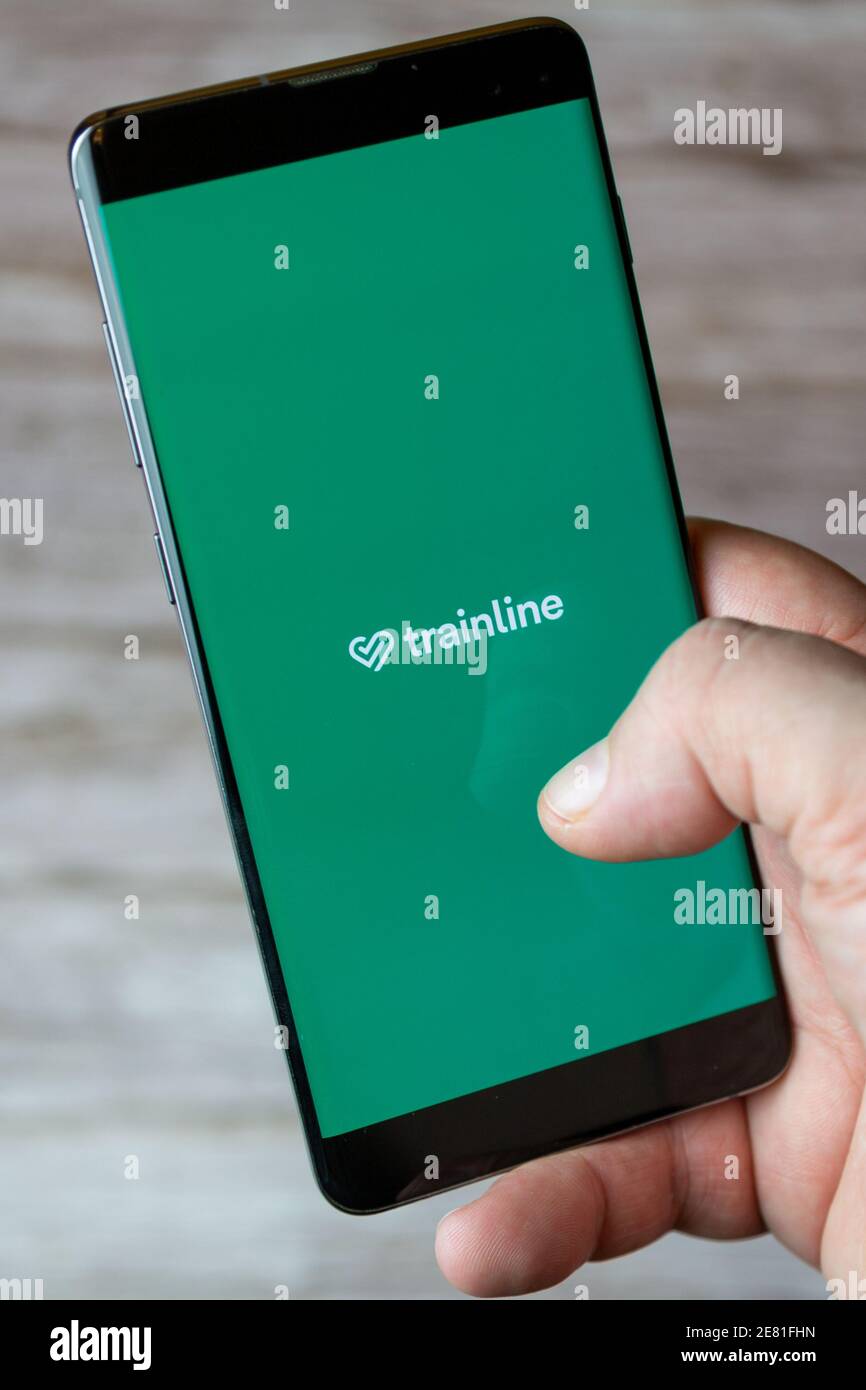A hand holding a mobile phone or cell phone with the Trainline app open ...