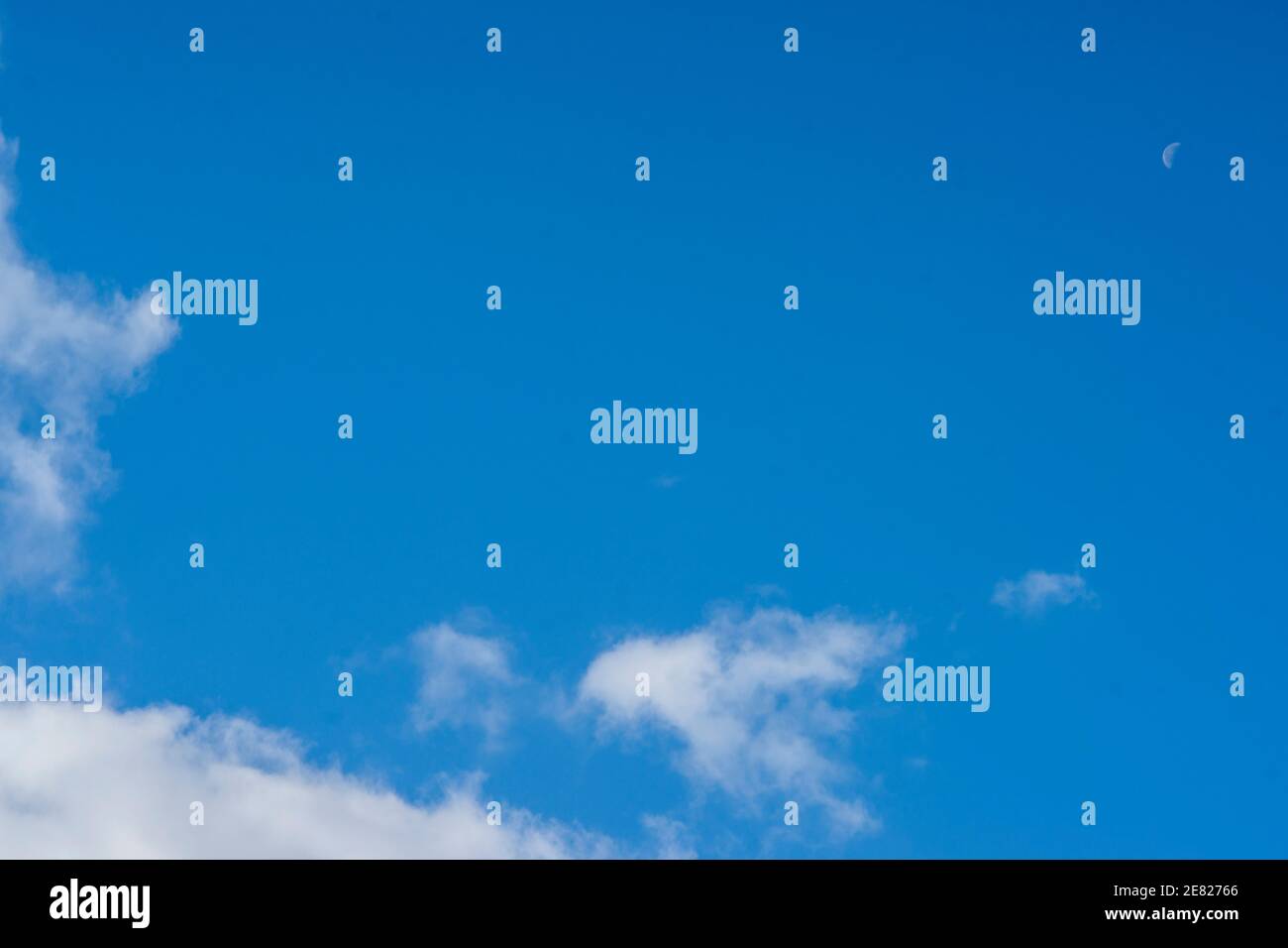 Bright tropical sky with cumulus clouds and a pale, half moon over ...