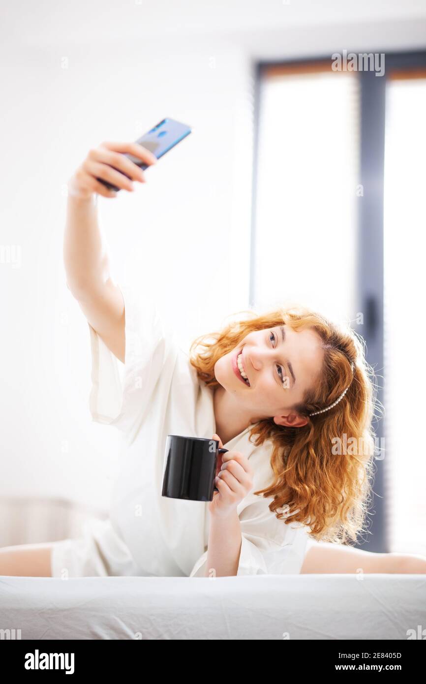 Casual careless girl at home using smart phone. Lying in bed scrolling ...