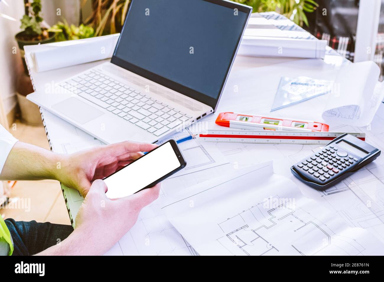 A male engineer hands using a mobile phone while working on blueprints ...