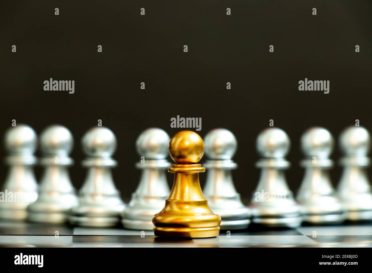 Gold pawn piece stand in fron of silver pawn team on black background ...