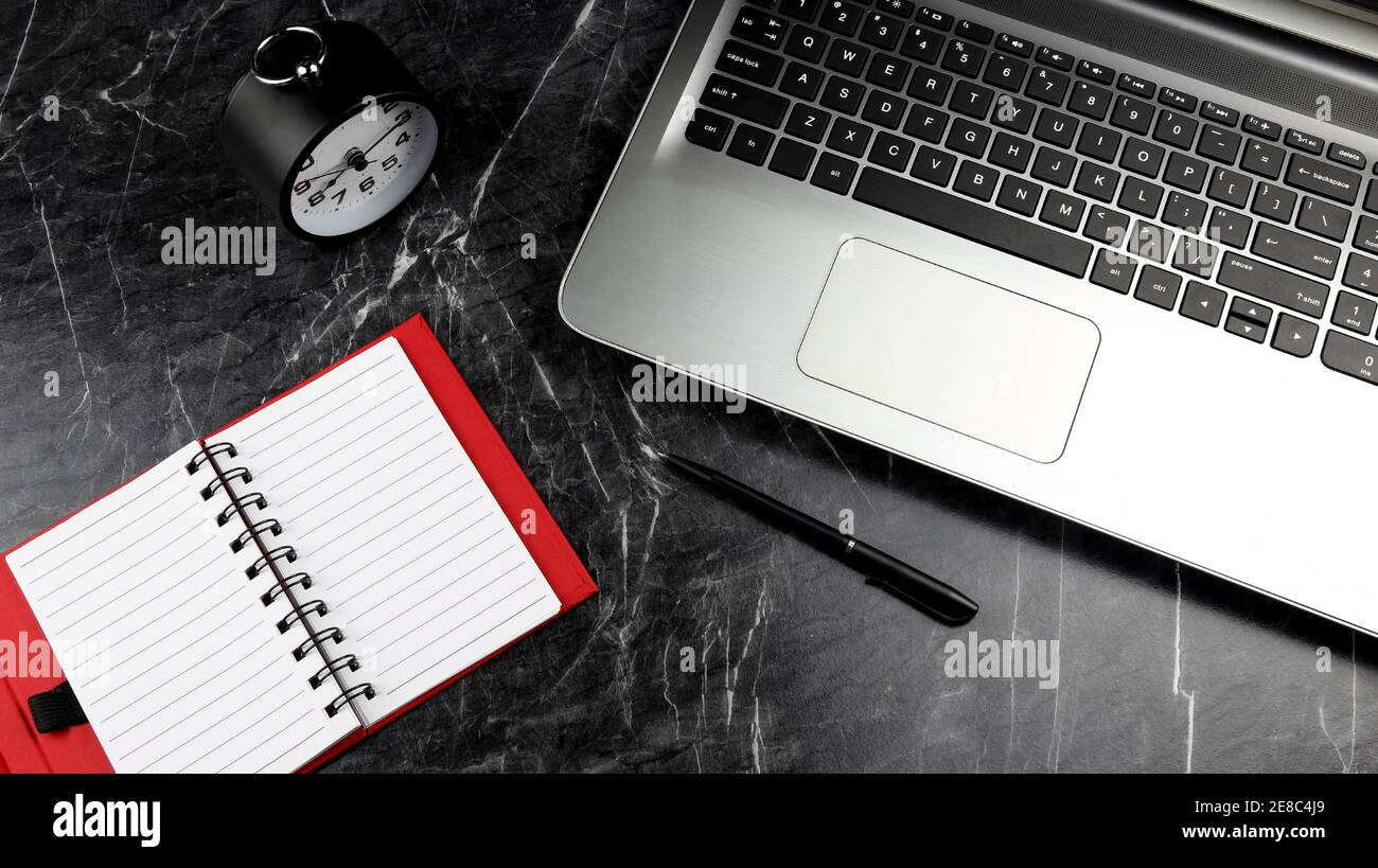 A laptop, clock and notebook on the black rough marble surface. Time ...
