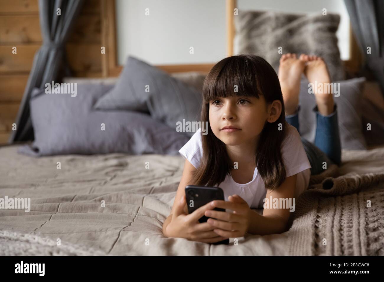 Close up dreamy little girl holding phone, lying on bed Stock Photo - Alamy