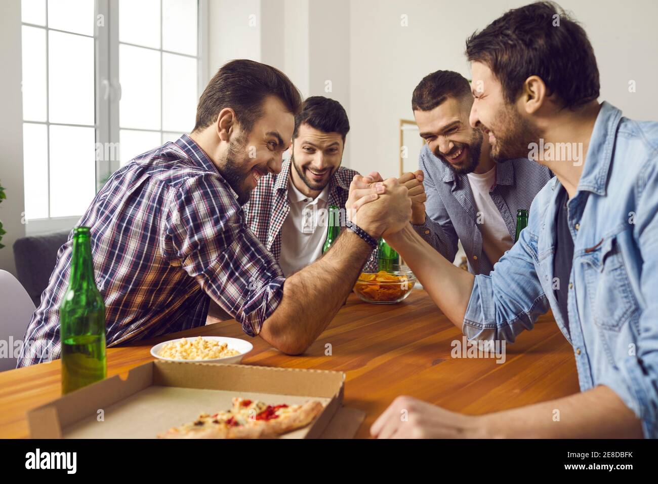 Group of friends watching two men arm-wrestling at fun party with pizza ...