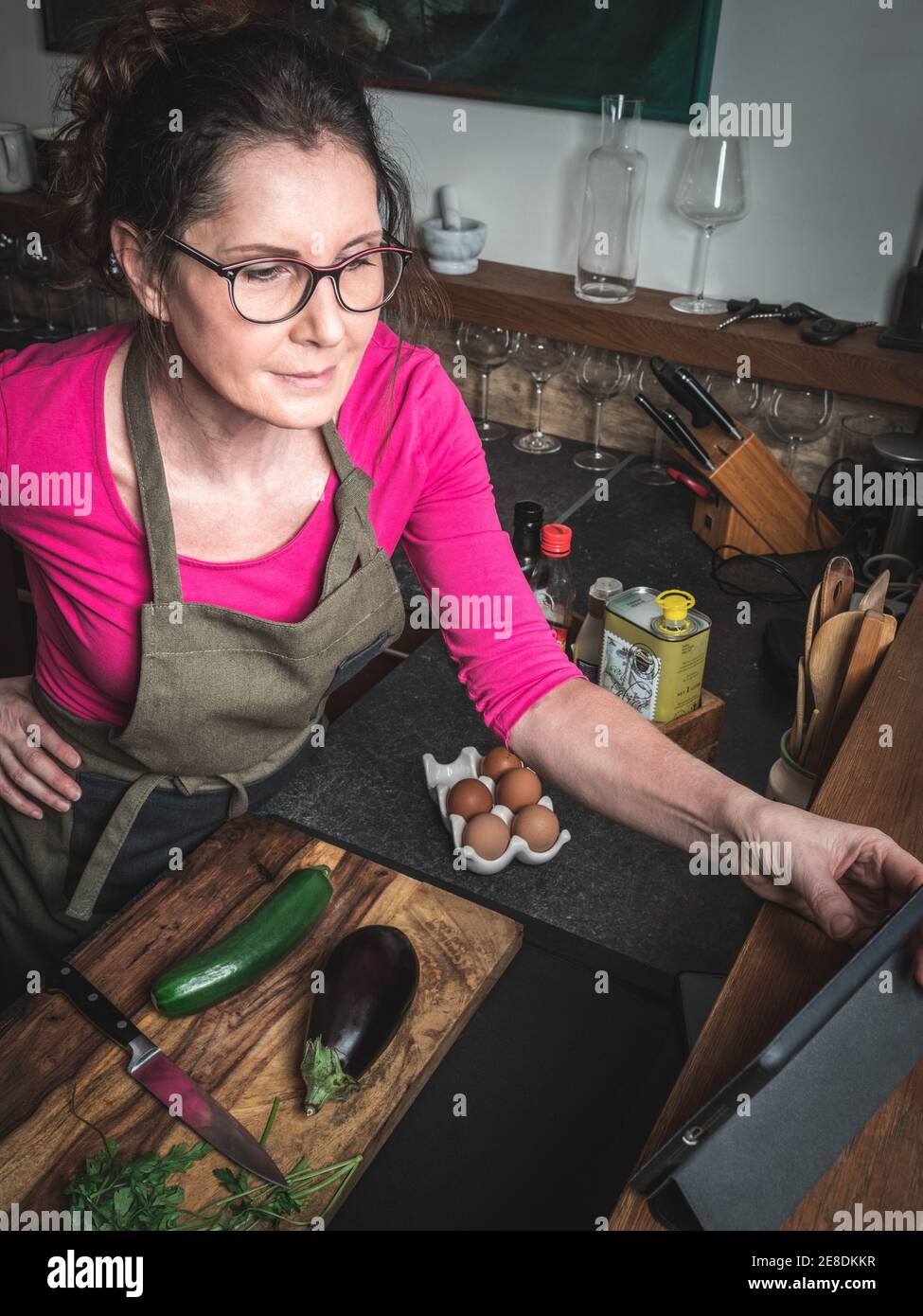 Caucasian middle aged woman in the kitchen follows recipe on digital ...