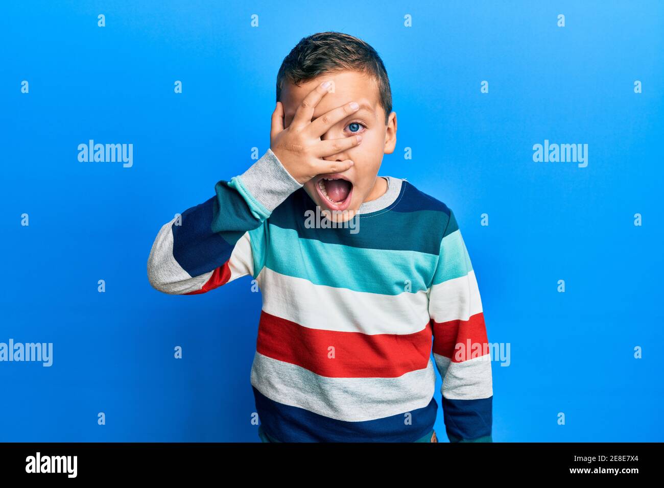 Little kid boy wearing striped sweater peeking in shock covering face ...