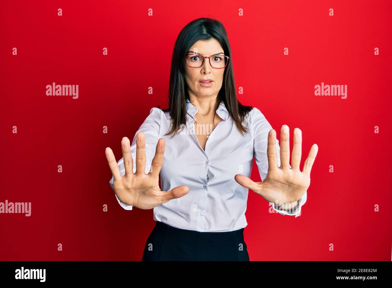 Young hispanic woman wearing business shirt and glasses afraid and ...
