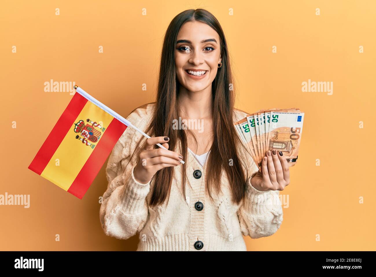 Beautiful brunette young woman holding spain flag and euros banknotes ...