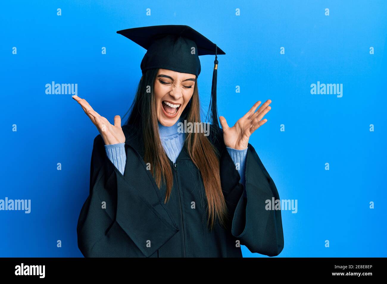 Beautiful brunette young woman wearing graduation cap and ceremony robe ...
