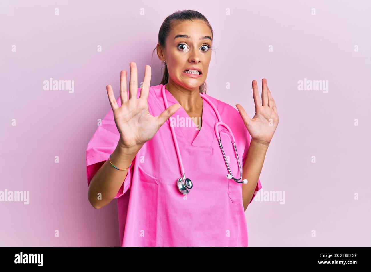 Young hispanic woman wearing doctor uniform and stethoscope afraid and ...