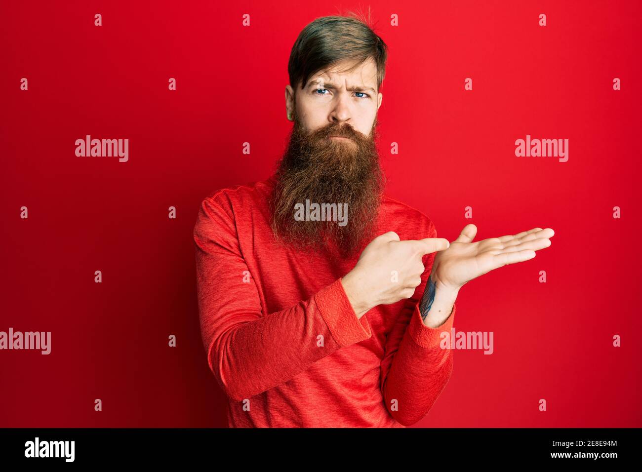 Redhead man with long beard pointing open palm with finger skeptic and ...