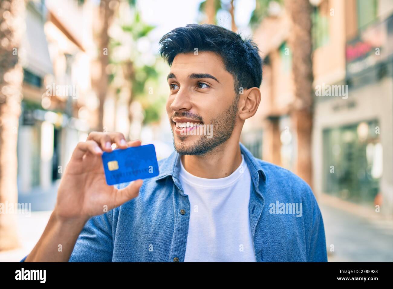 Young latin man smiling happy holding credit card walking at the city ...