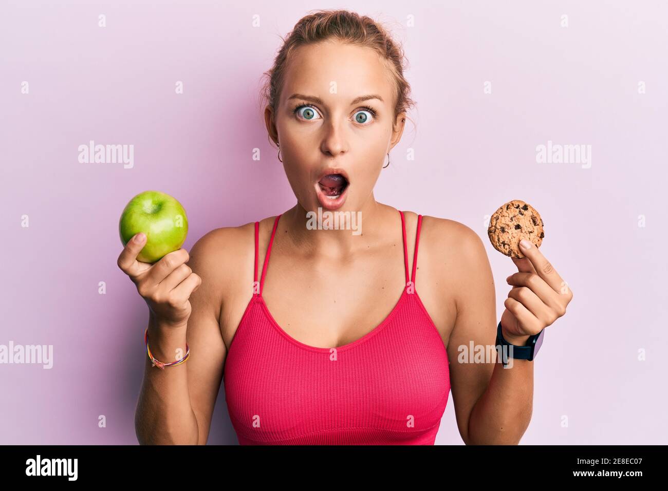 Beautiful caucasian woman holding green apple and cookie afraid and ...