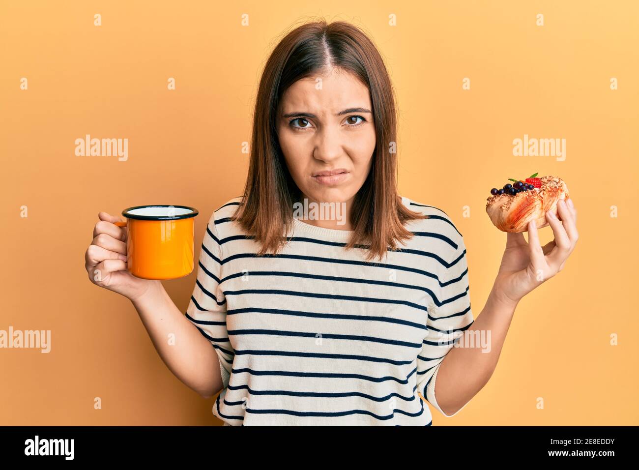 Young beautiful woman drinking coffee and eating pastry skeptic and ...