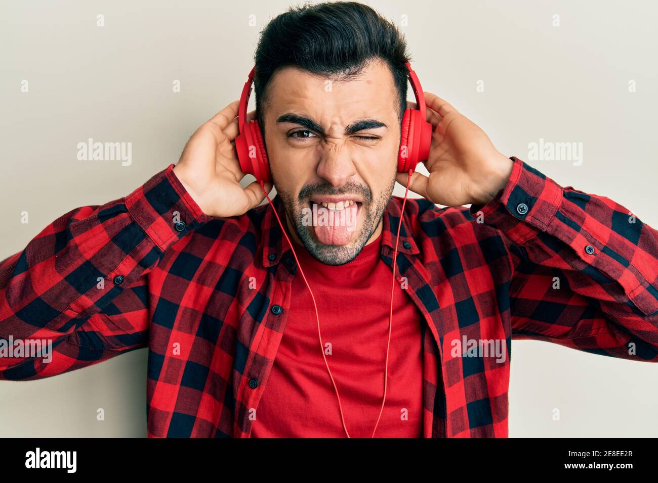 Young hispanic man listening to music using headphones sticking tongue ...