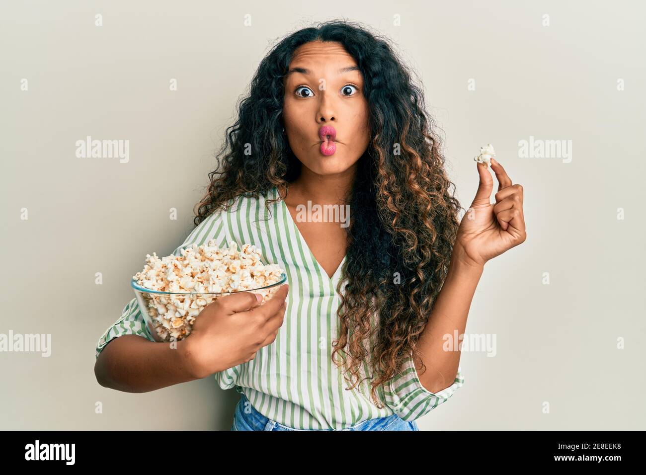 Young latin woman eating popcorn making fish face with mouth and ...