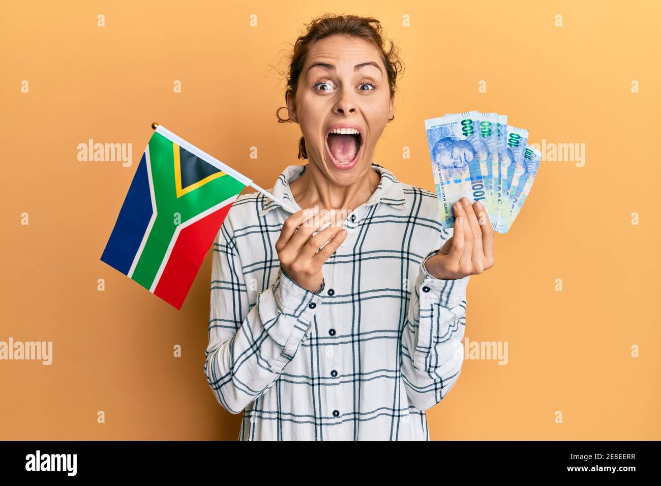 Young brunette woman holding south africa flag and rand banknotes ...