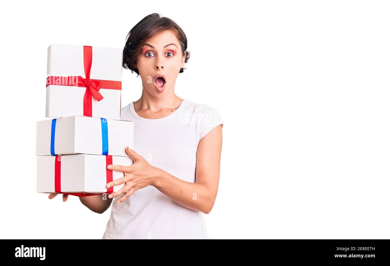 Beautiful young woman with short hair holding gifts scared and amazed ...