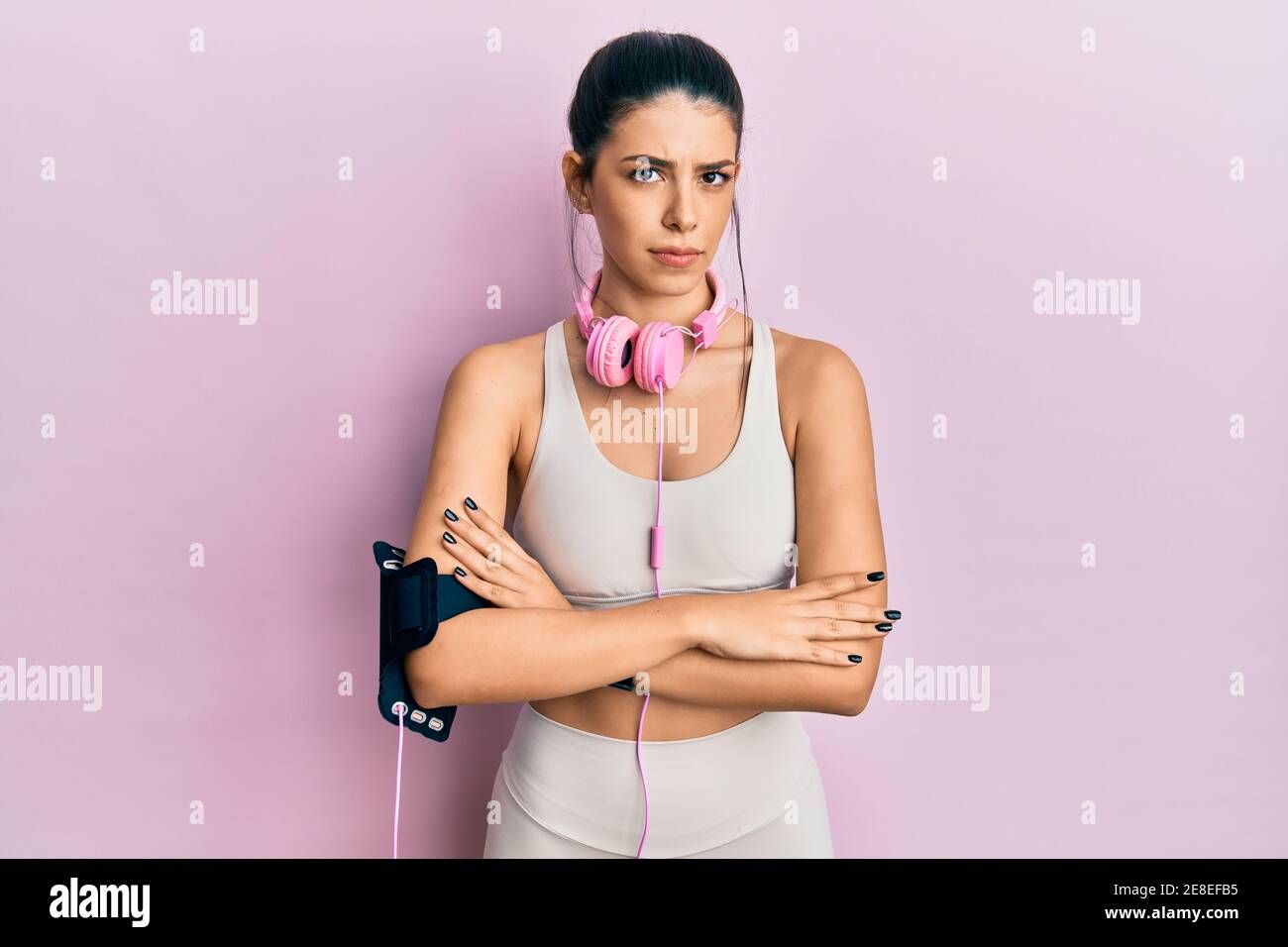 Young hispanic woman wearing gym clothes and using headphones skeptic ...