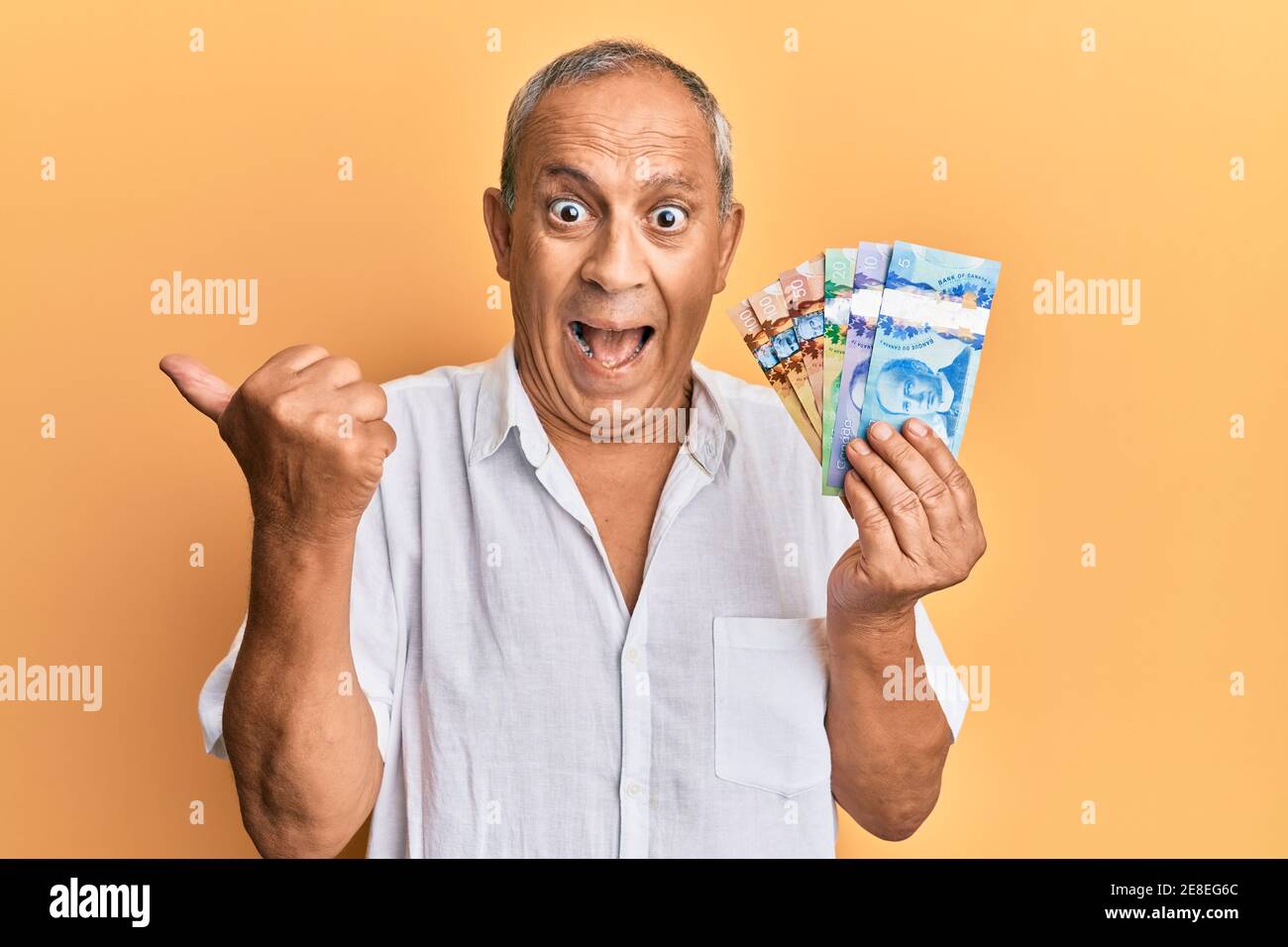 Handsome mature man holding canadian dollars pointing thumb up to the ...