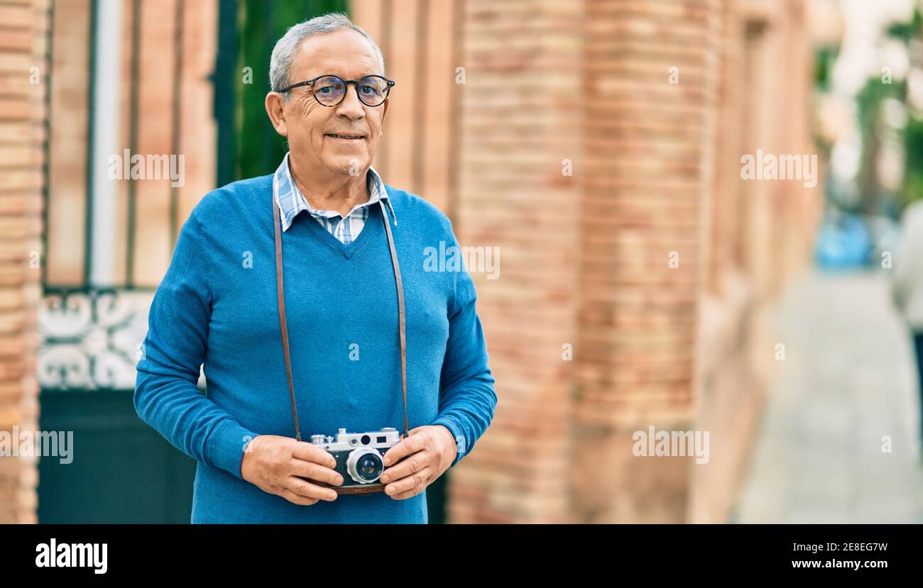Senior grey-haired tourist man smiling happy using vintage camera at ...