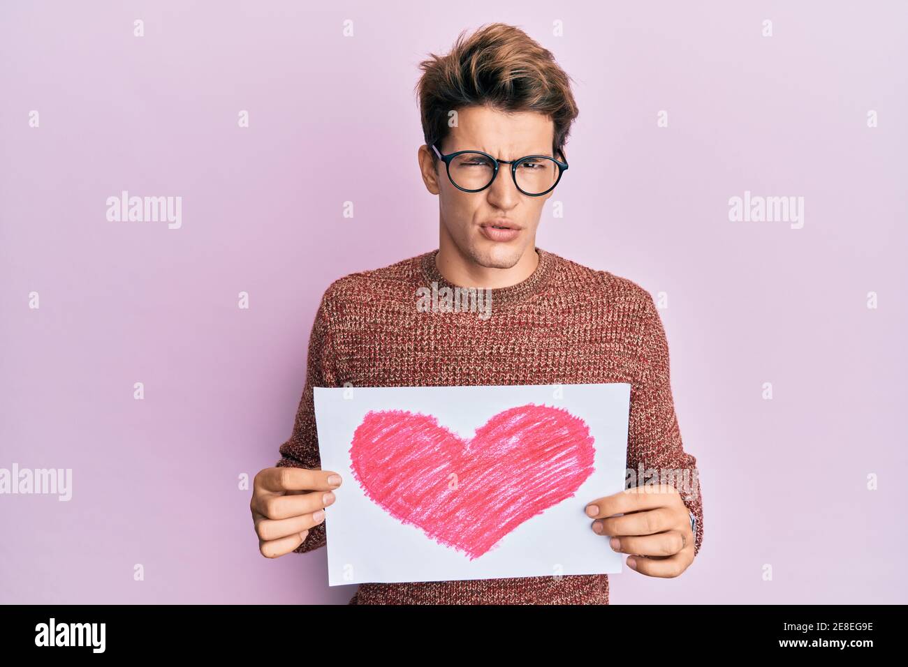 Handsome caucasian man holding heart draw skeptic and nervous, frowning ...