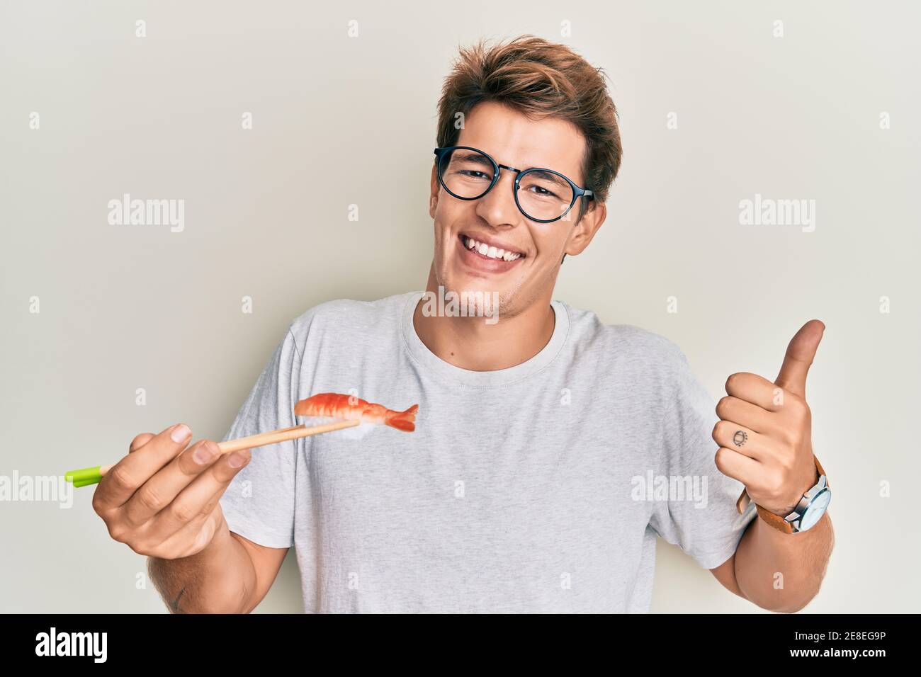 Handsome caucasian man eating prawn sushi using chopsticks smiling ...