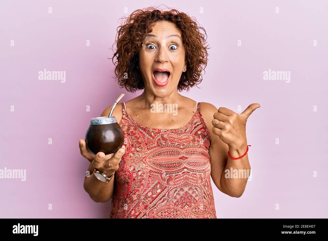 Beautiful middle age mature woman drinking mate infusion pointing thumb ...