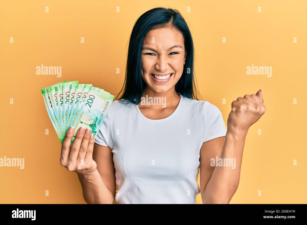 Beautiful hispanic woman holding 200 russian ruble banknotes screaming ...