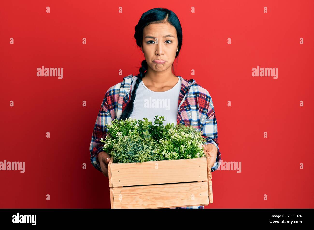 Beautiful hispanic woman holding wooden plant pot depressed and worry ...