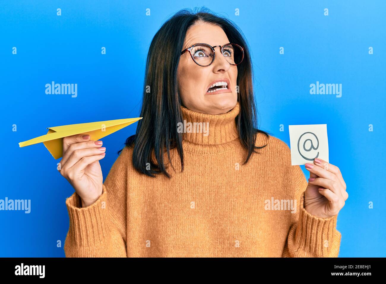 Middle age brunette woman holding email symbol and paper plane angry ...