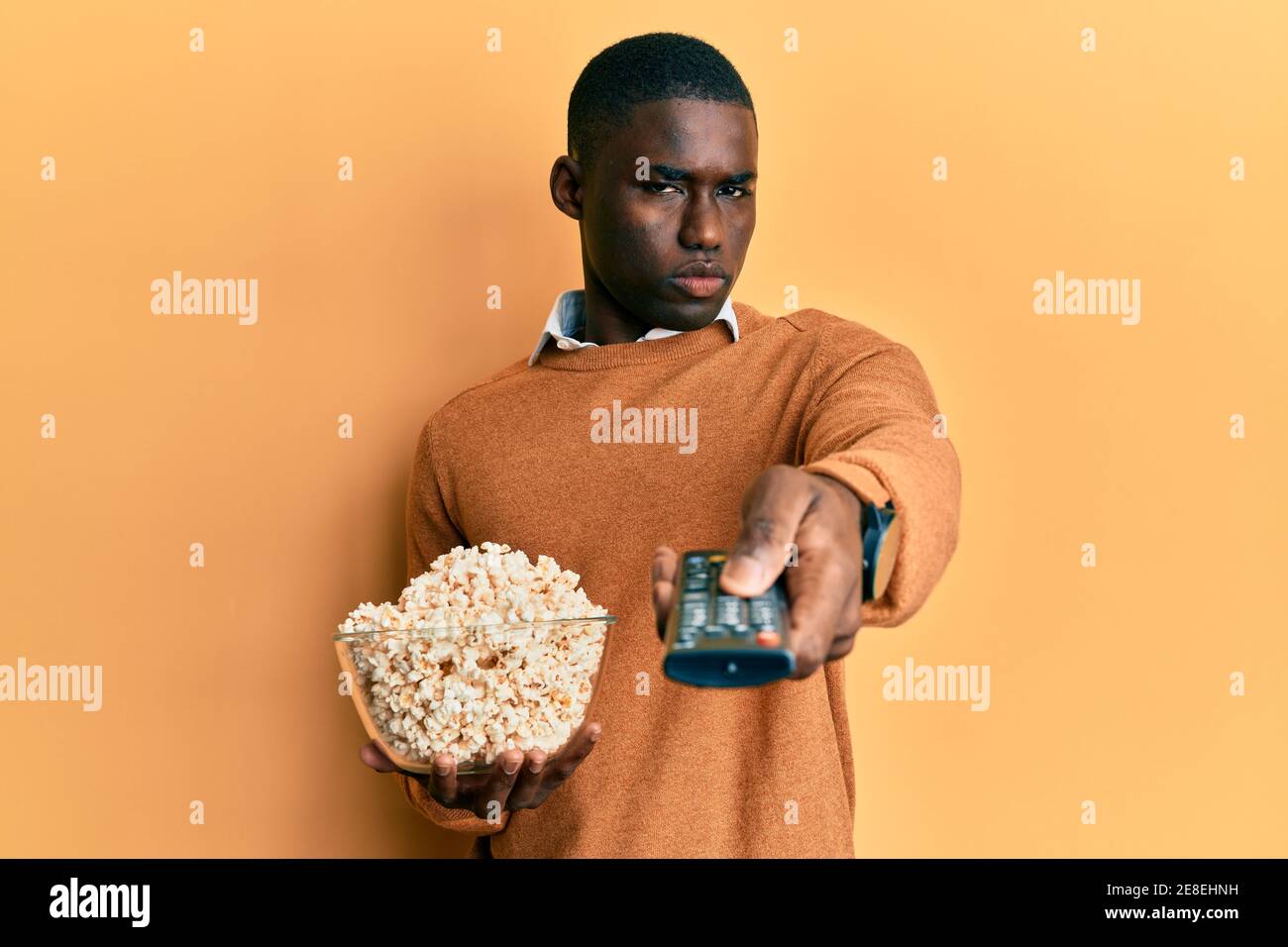 Young african american man holding television remote control eating ...