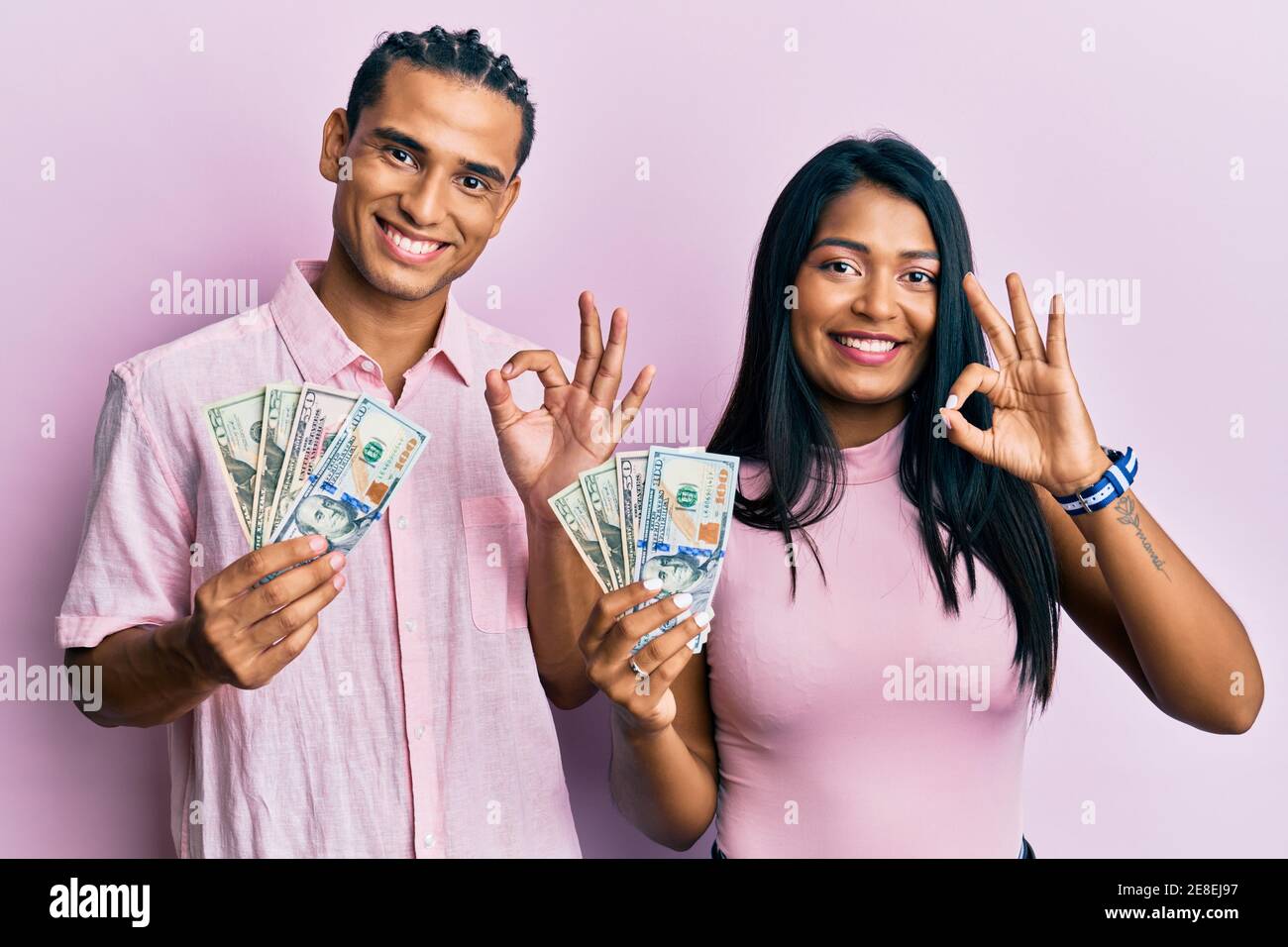 Young latin couple holding dollars doing ok sign with fingers, smiling ...