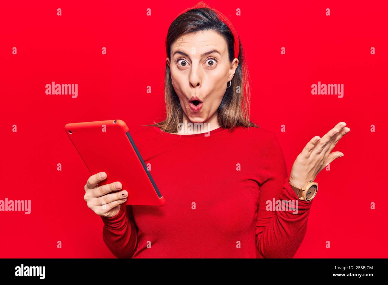 Young beautiful woman holding touchpad scared and amazed with open ...