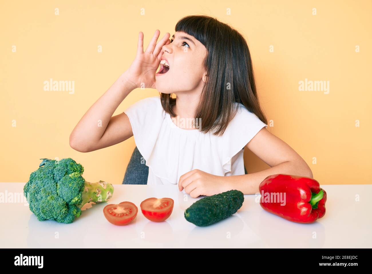 Young little girl with bang sitting on the table with veggies shouting ...