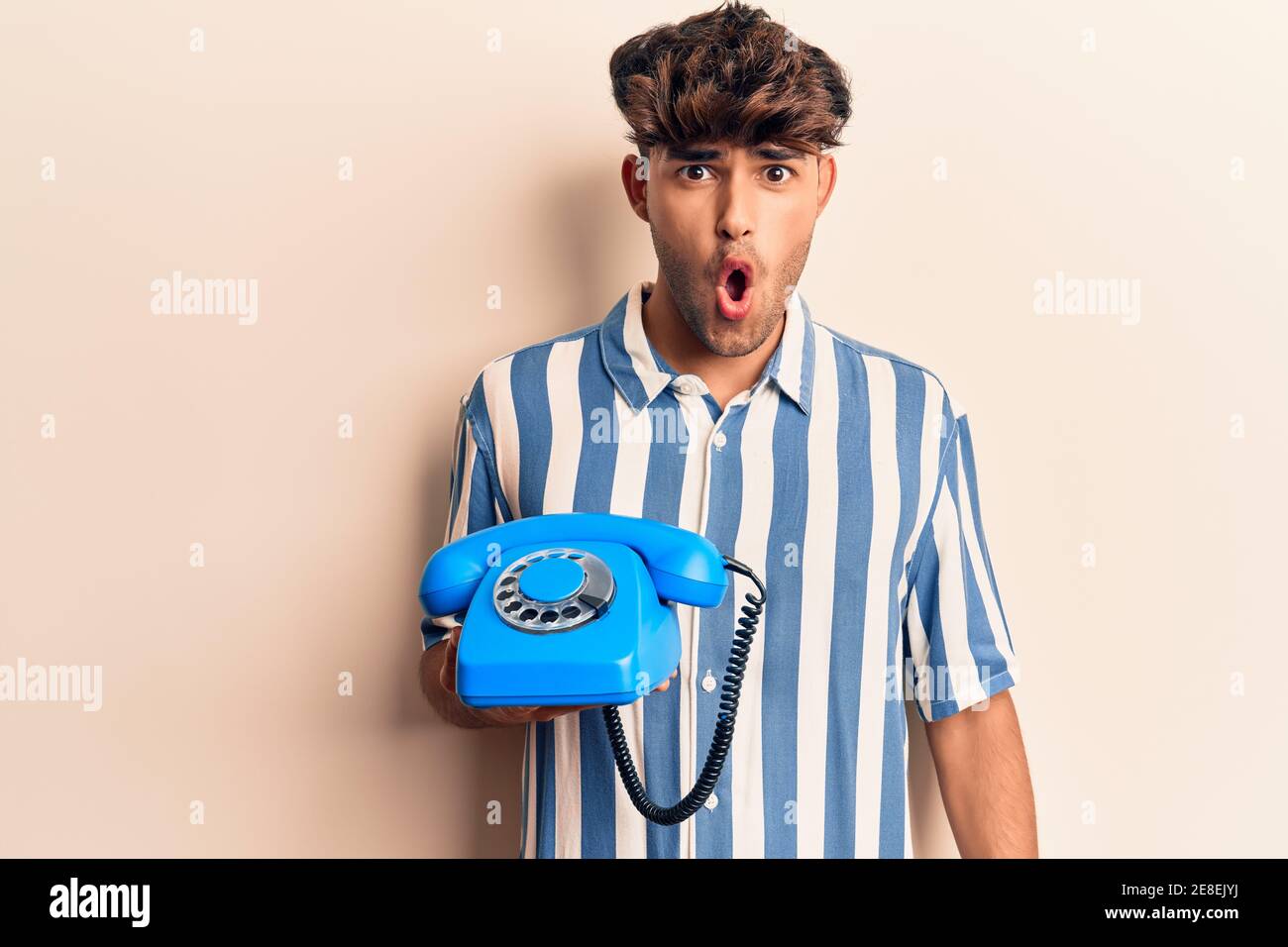 Young hispanic man holding vintage telephone scared and amazed with ...