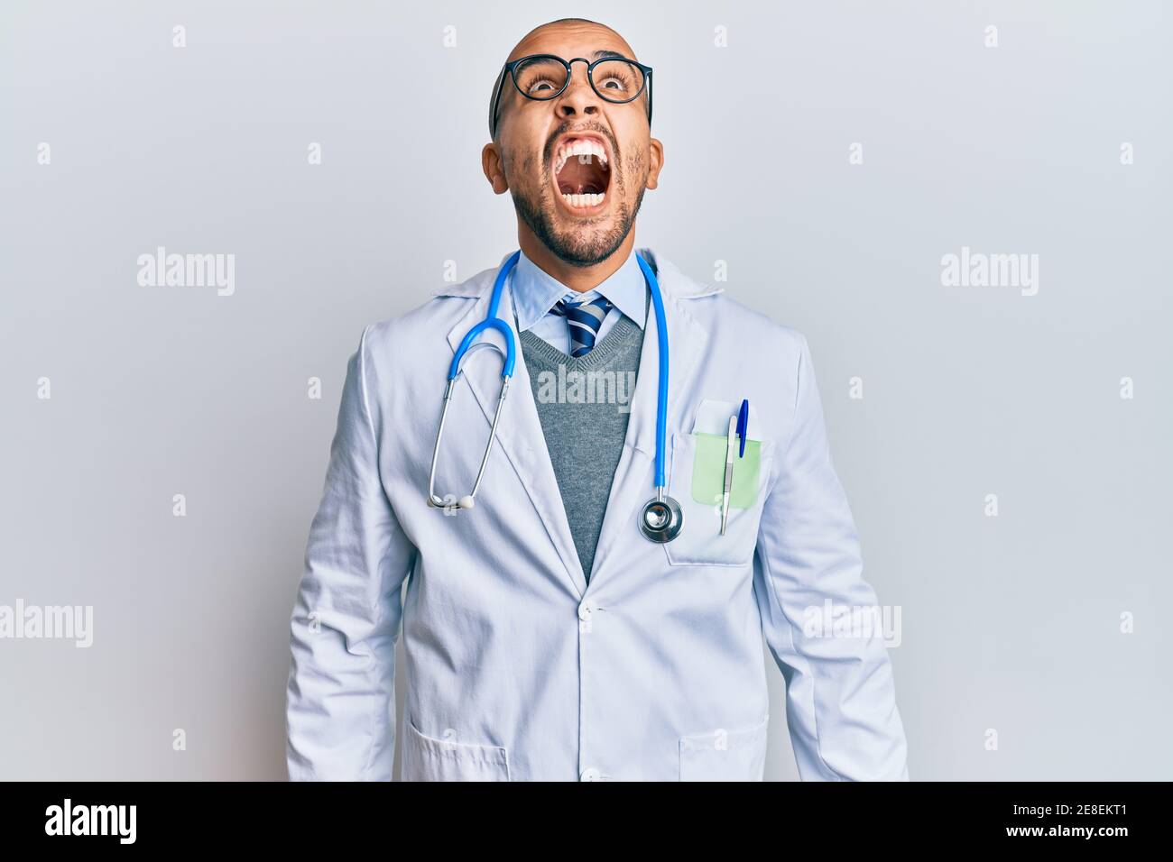 Hispanic adult man wearing doctor uniform and stethoscope angry and mad ...