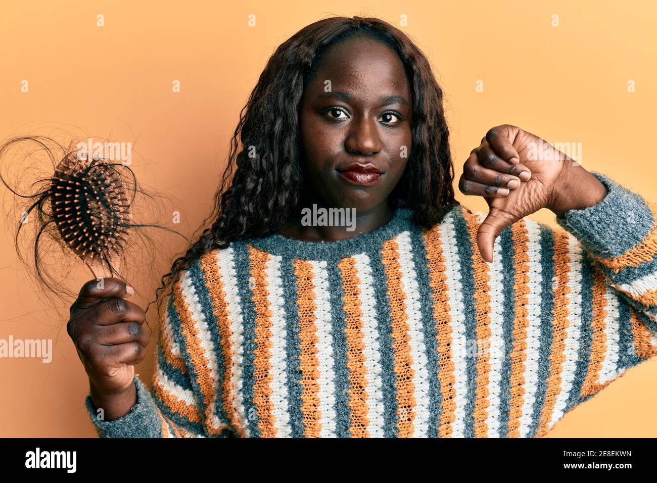 African young woman holding comb loosing hair with angry face, negative ...