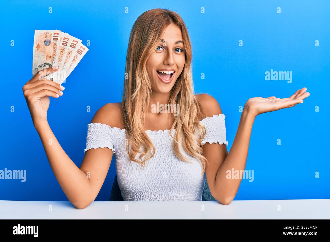 Beautiful blonde young woman holding 10 united kingdom pounds banknotes ...