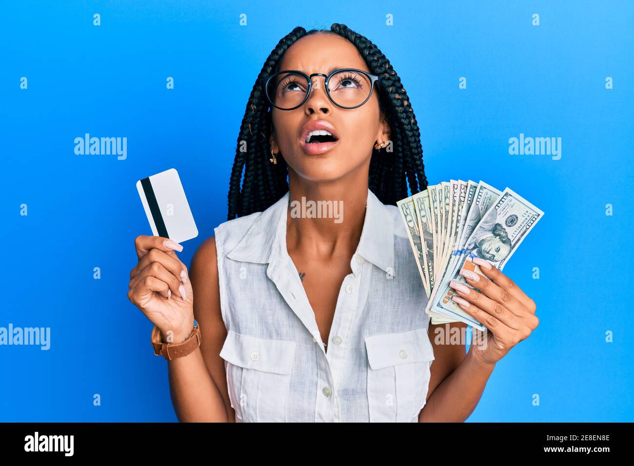 Beautiful hispanic woman holding dollars and credit card angry and mad ...