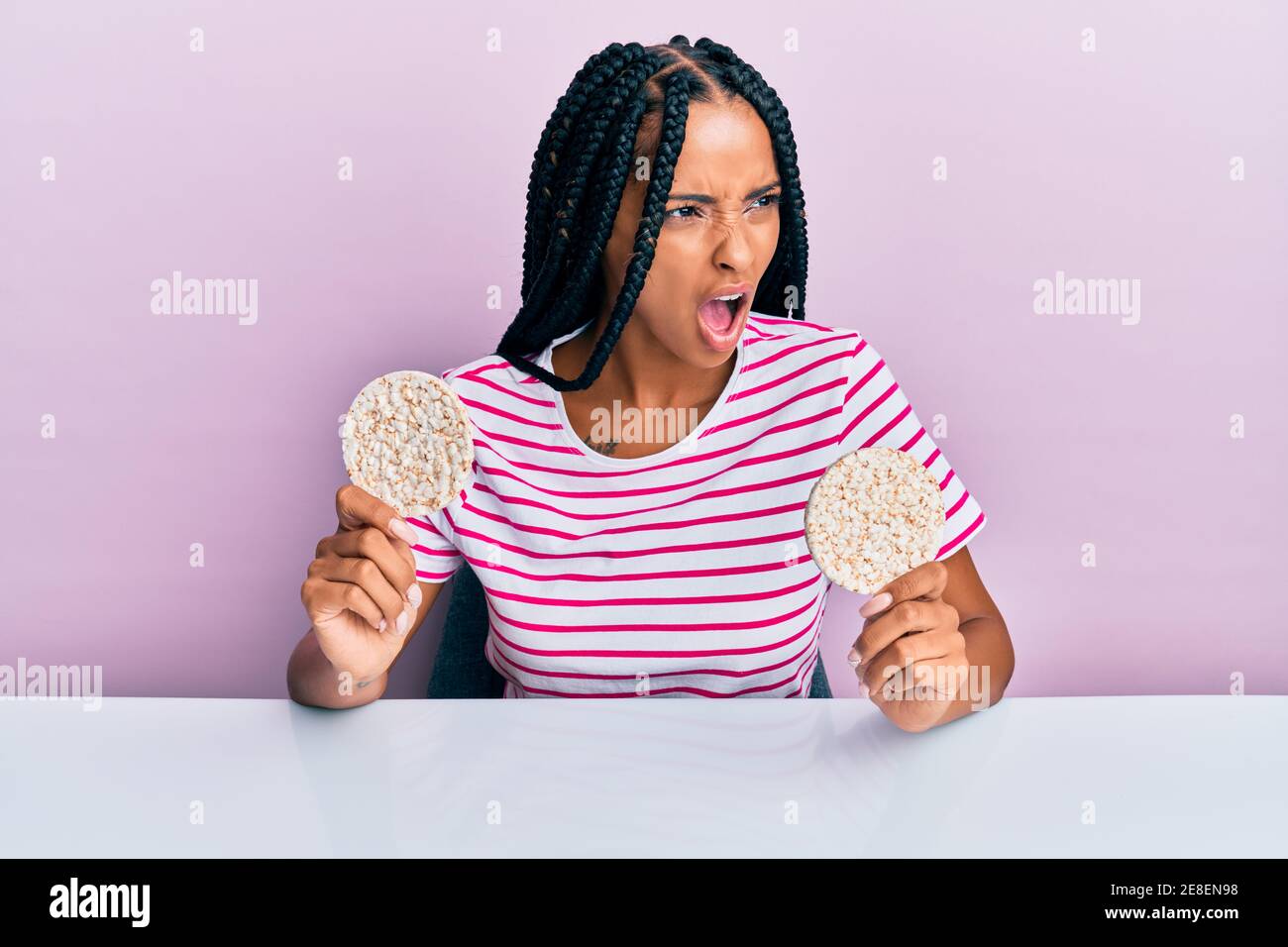 Beautiful hispanic woman eating healthy rice crackers angry and mad ...