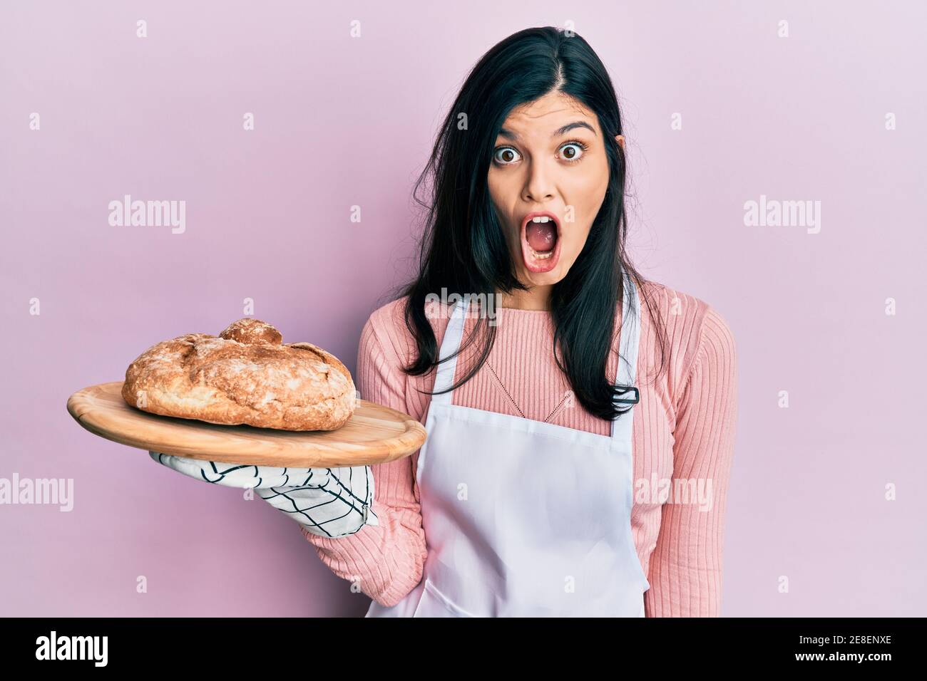 Young hispanic woman wearing baker uniform holding homemade bread ...